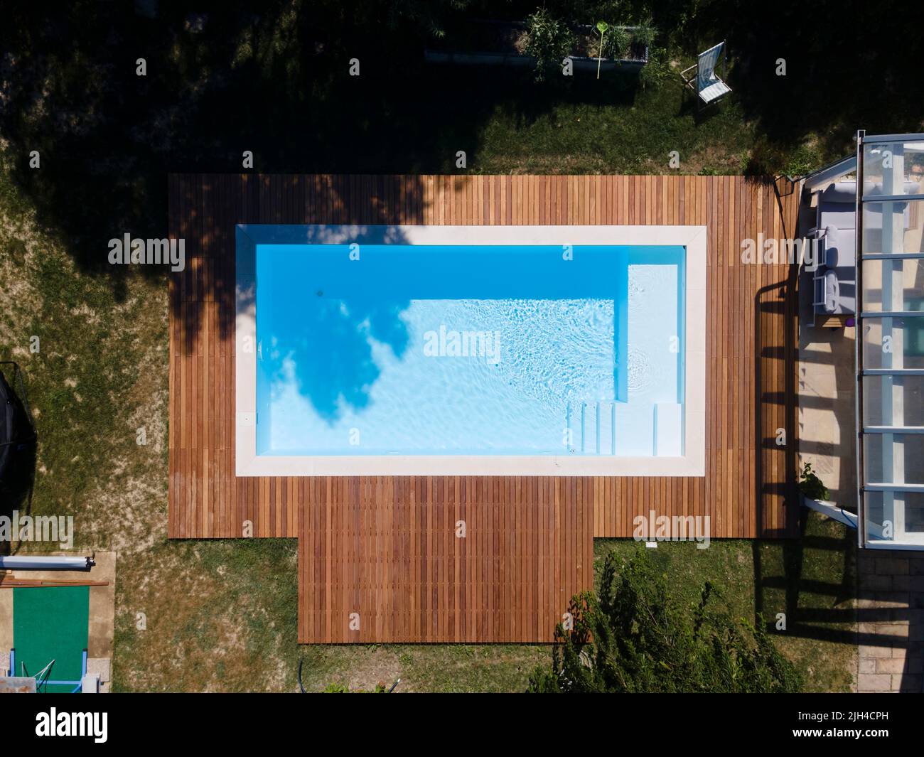 Drone flight over pool with nice wooden terrace surrounded by green ...