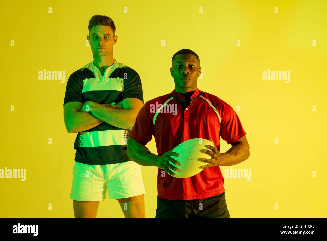 Portrait of diverse male rugby players with rugby ball over yellow ...
