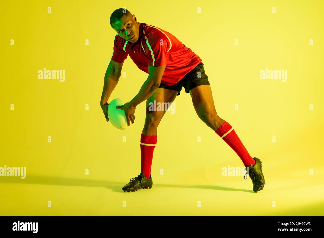 African american male rugby player with rugby ball over yellow lighting ...