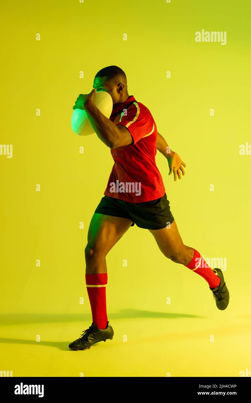 African american male rugby player running with rugby ball over yellow ...