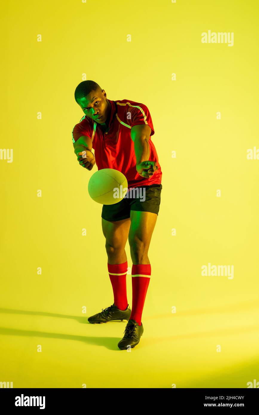 African american male rugby player with rugby ball over yellow lighting ...