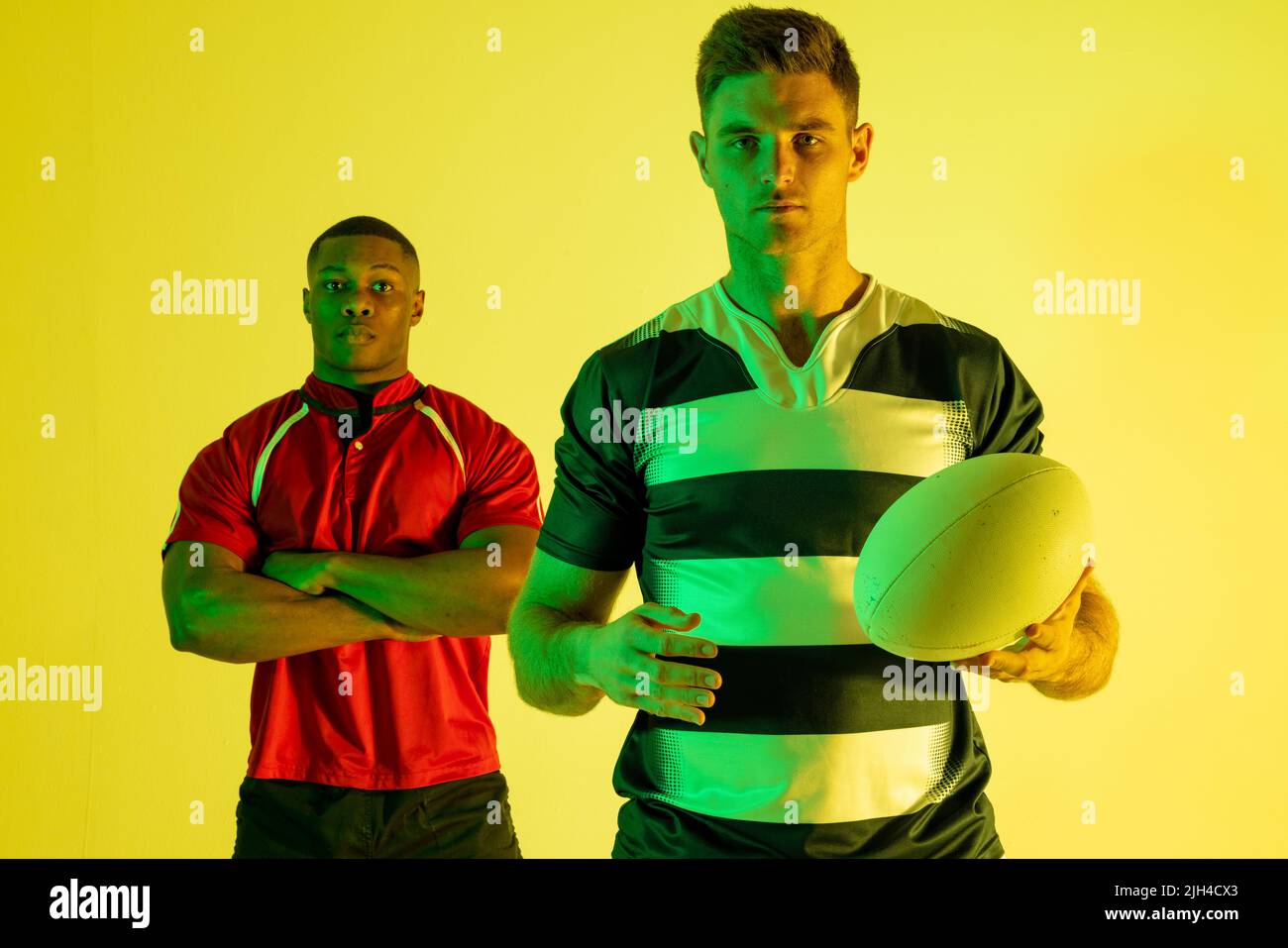 Portrait of diverse male rugby players with rugby ball over yellow ...