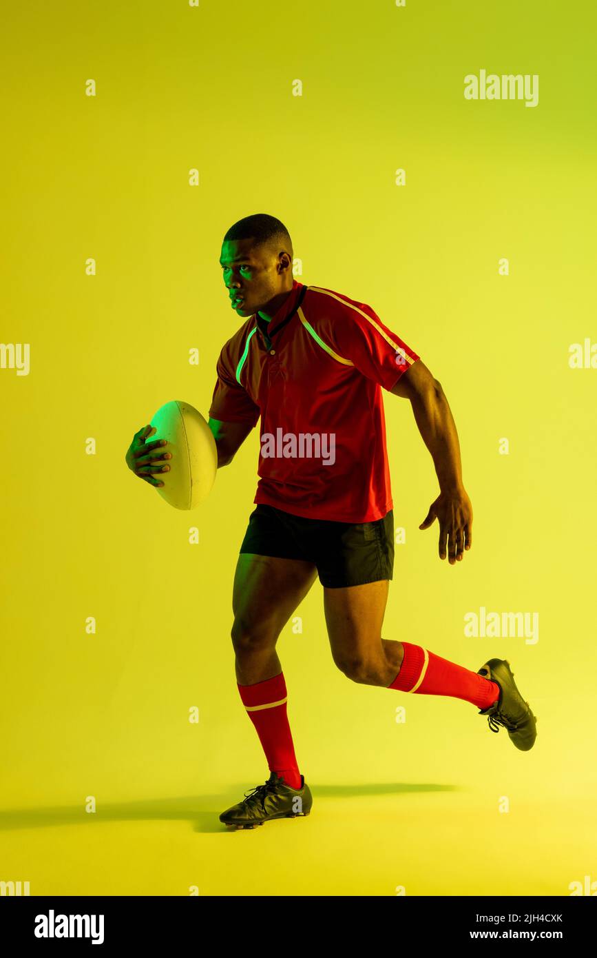 African american male rugby player running with rugby ball over yellow ...