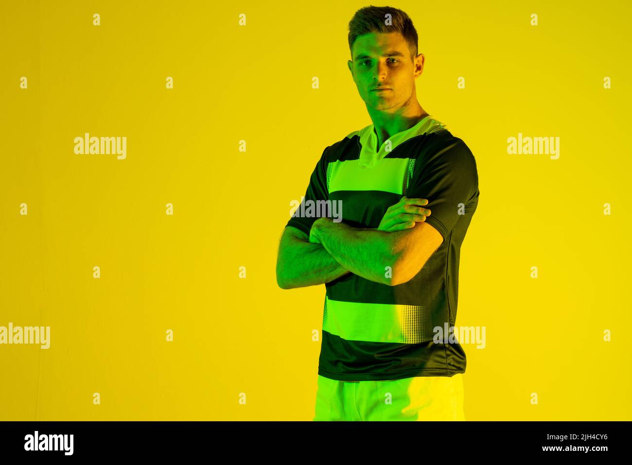 Portrait of caucasian male rugby player with arms crossed over orange ...