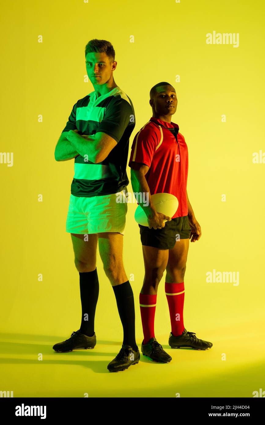 Portrait of diverse male rugby players with rugby ball over yellow ...