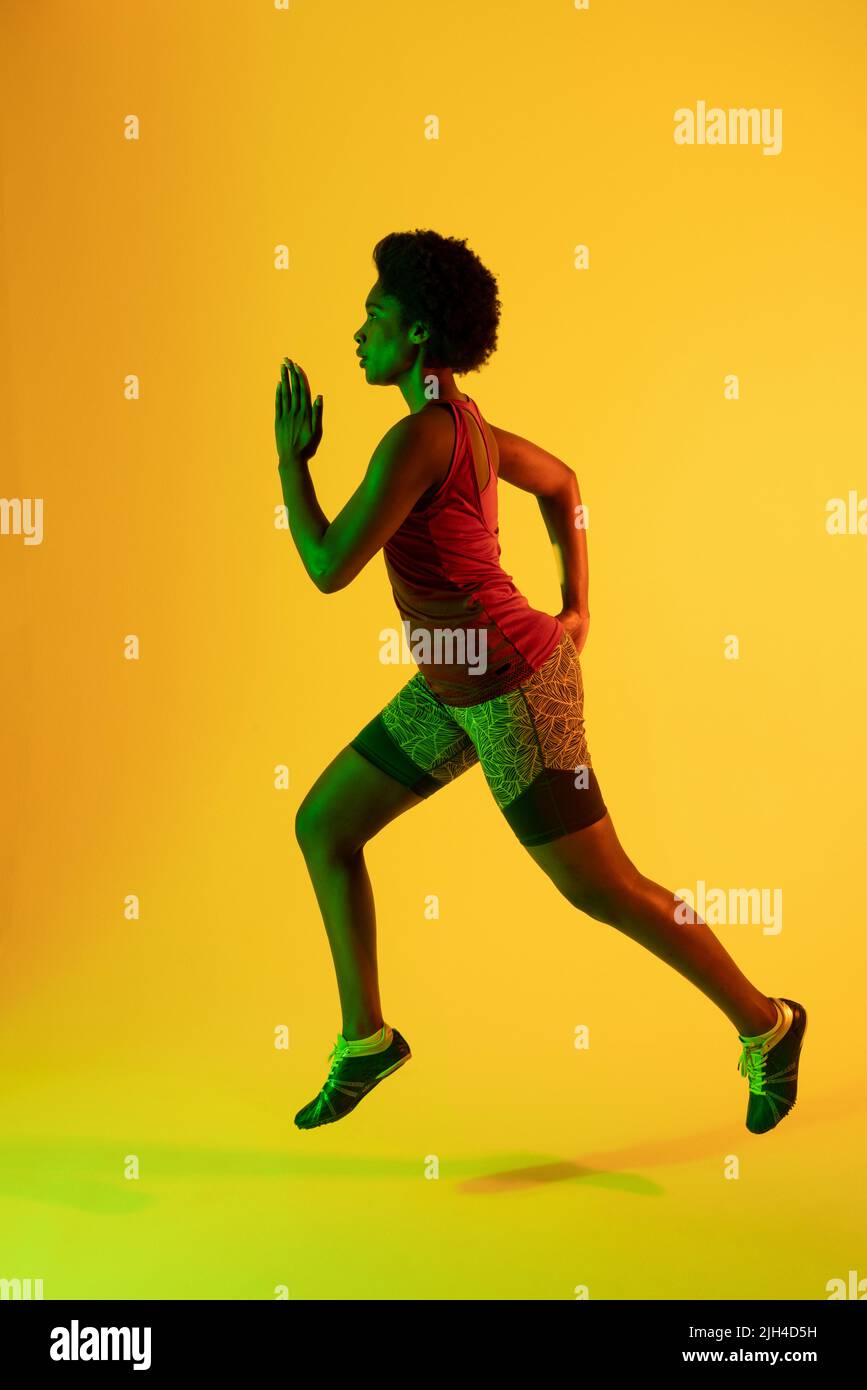 Vertical image of african american female athlete running in yellow ...