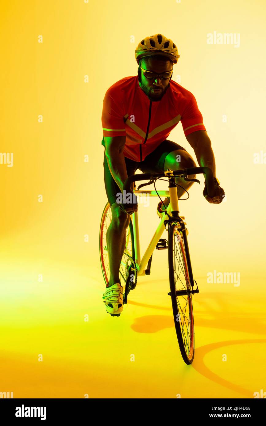 Vertical image of african american male cyclist riding bike in yellow ...