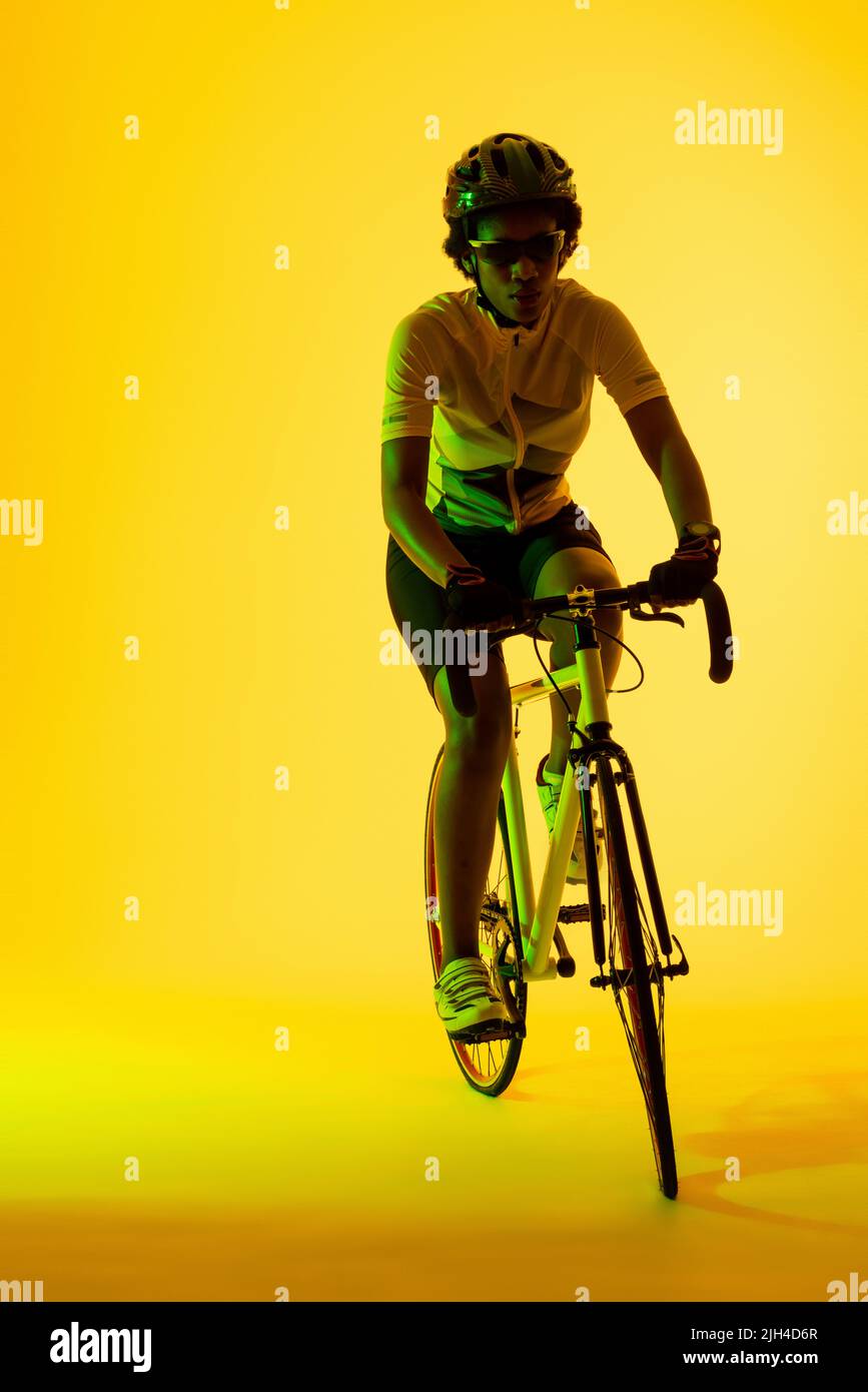 Vertical image of african american female cyclist riding bike in yellow ...