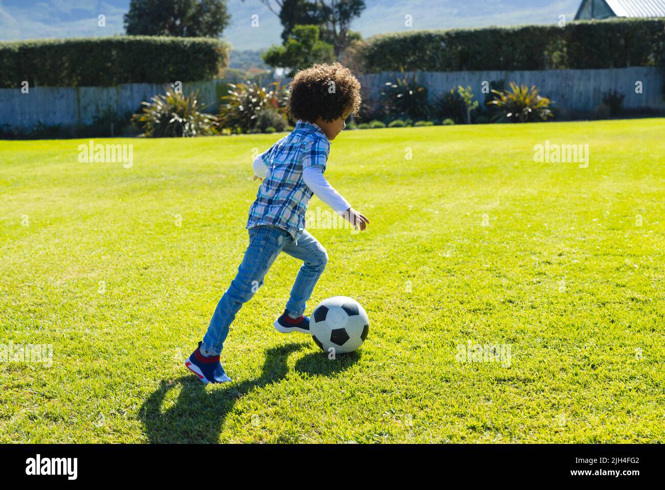 Side view of biracial boy with afro hair running and kicking soccer ...
