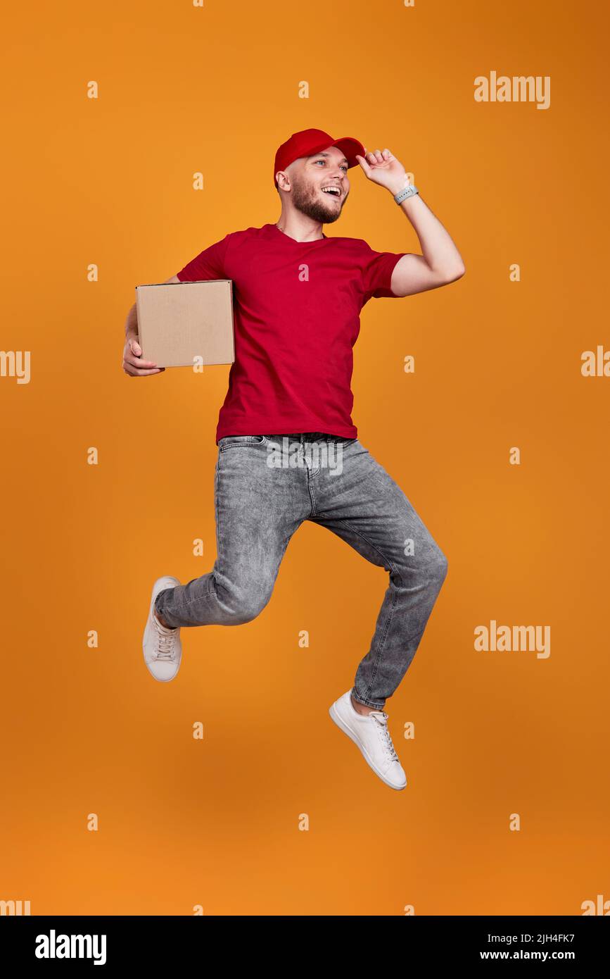 Delivery man in red cap holding cardboard box and jumping Stock Photo ...
