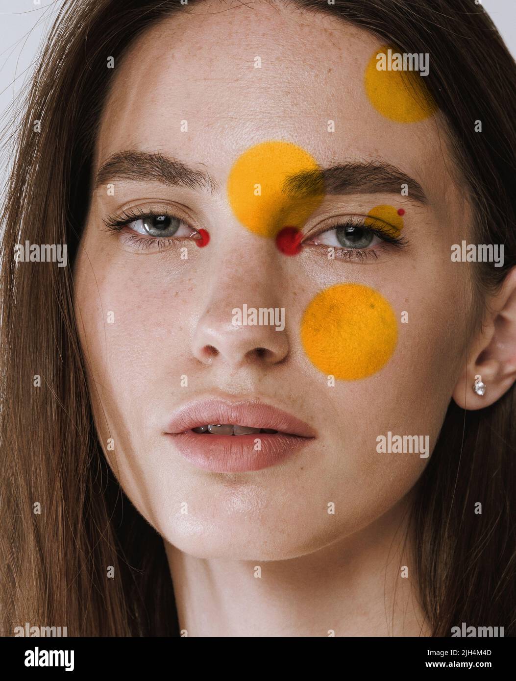 Close-up portrait of beautiful young woman with yellow and red dye dots ...