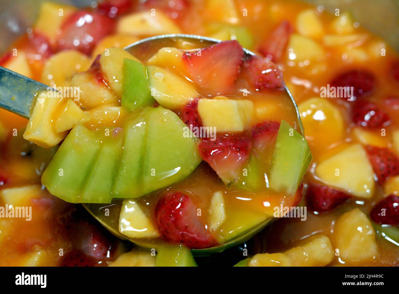 A ladle of fruit salad made of slices of bananas, strawberry ...