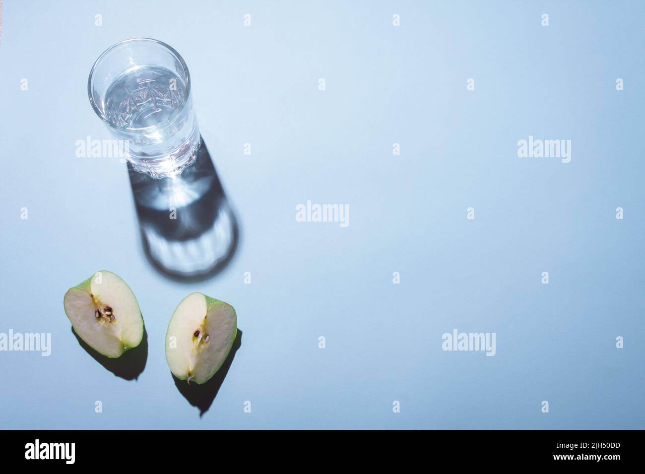 Glass of water and pieces of apple on blue background Stock Photo - Alamy