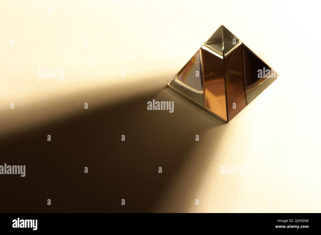 Minimalist still life image of a shiny pyramid in warm color tone ...