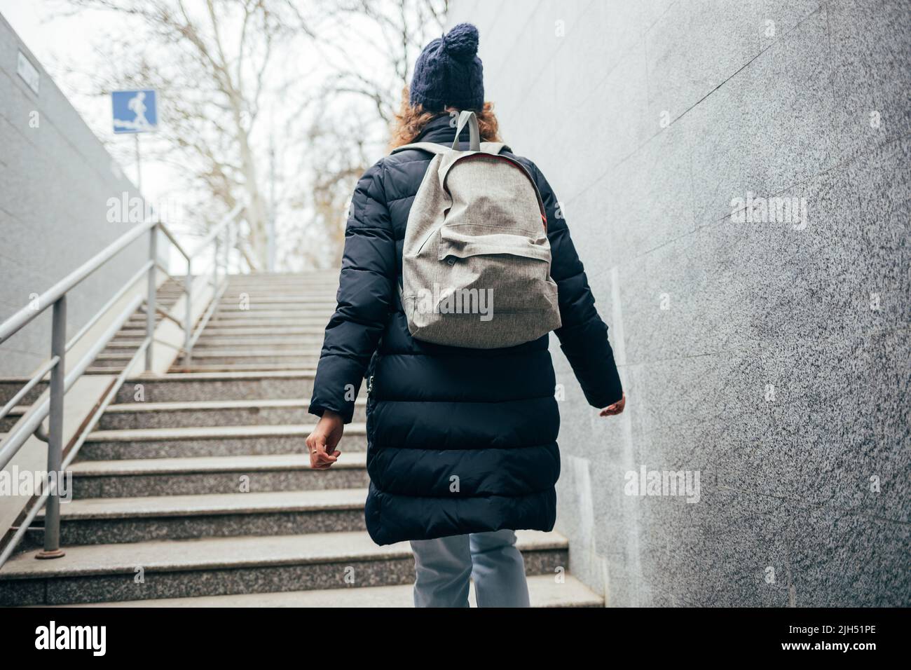 Woman goes up stairs. Rear view young woman wearing winter down jacket ...