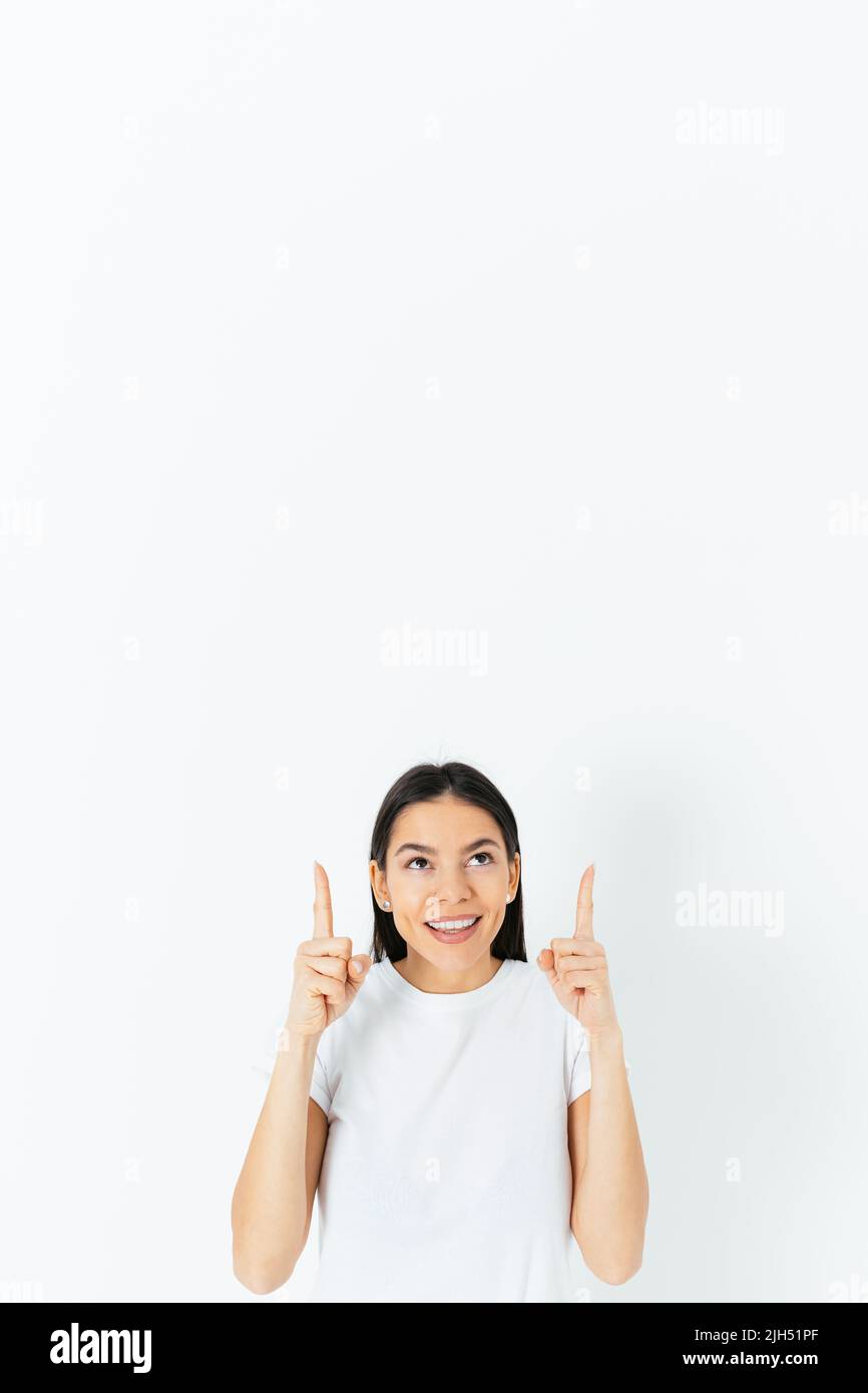 Happy young woman pointing her forefingers up and looking above, white ...
