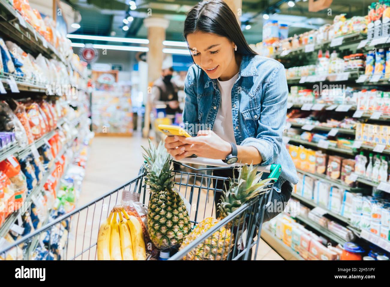 Happy young woman shopping for groceries in supermarket standing near ...