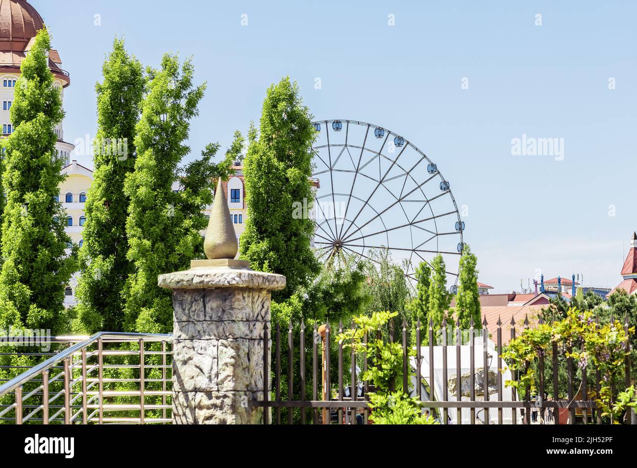 The Ferris wheel is visible from behind well-groomed park trees and ...