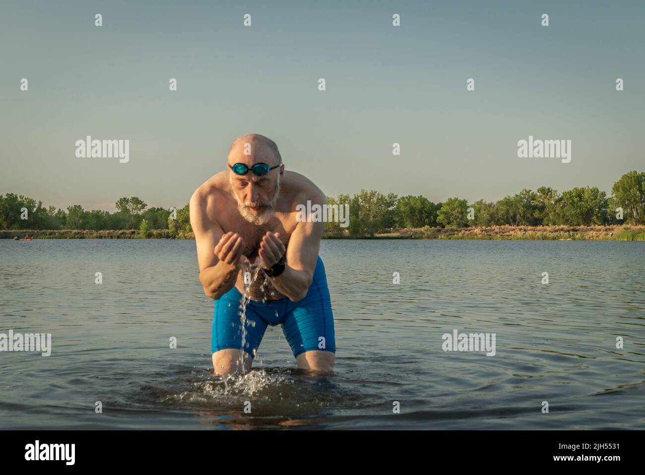 athletic, overweight senior male swimmer splashing himself in a lake in ...
