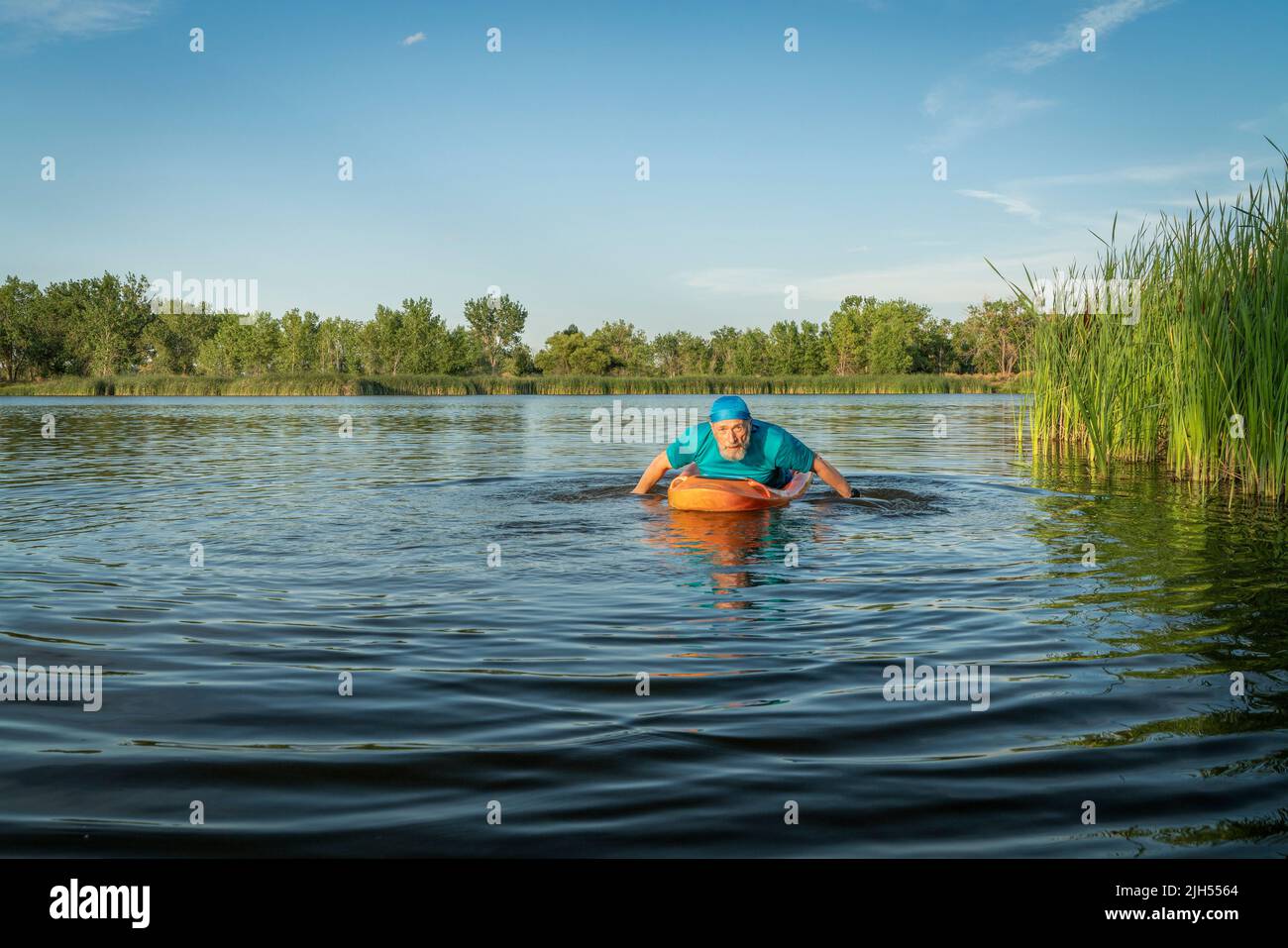 athletic, senior man is paddling a prone kayak on a lake in Colorado ...