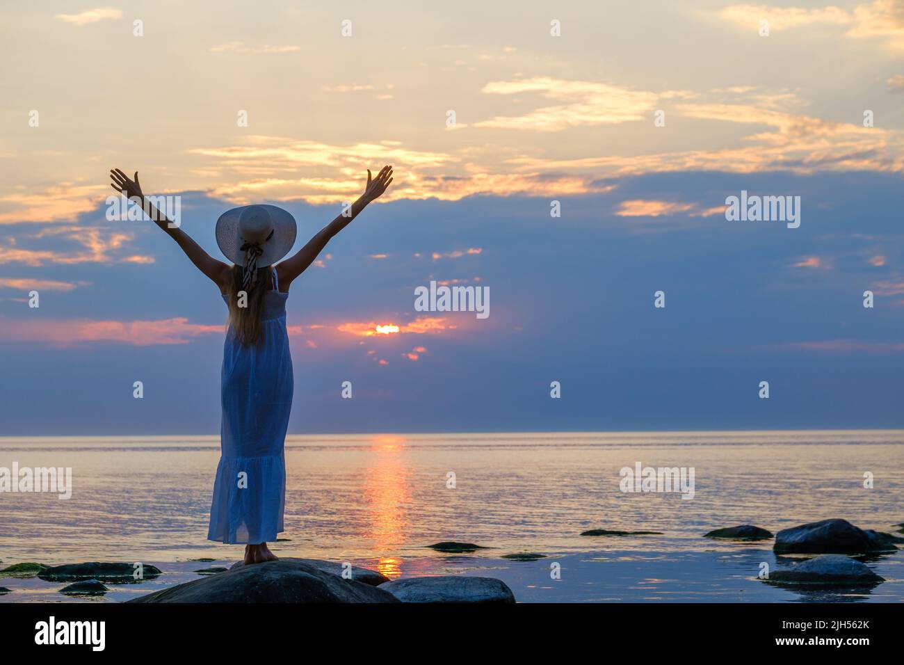 Back view of anonymous female in white dress standing on coast near sea ...