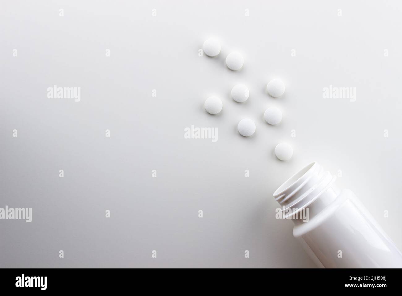 Round white pills spilled out of the white plastic jar in the lower ...