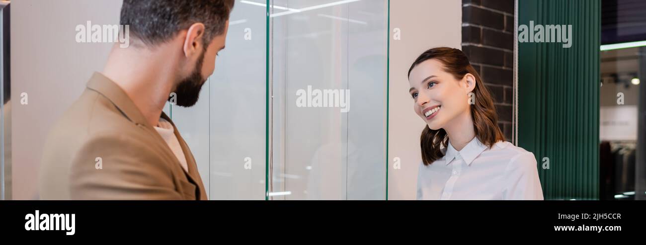 Positive seller looking at blurred client near glass showcase in ...