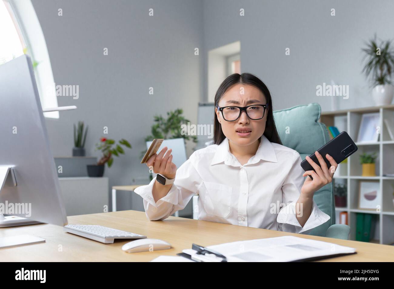 Fraud. Upset young beautiful Asian woman holding phone and credit card ...