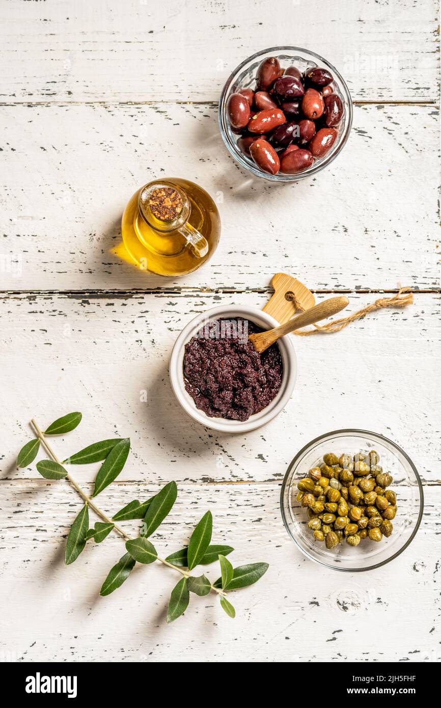 Olive pate in ramequin bowl and basic ingredients on white wooden ...