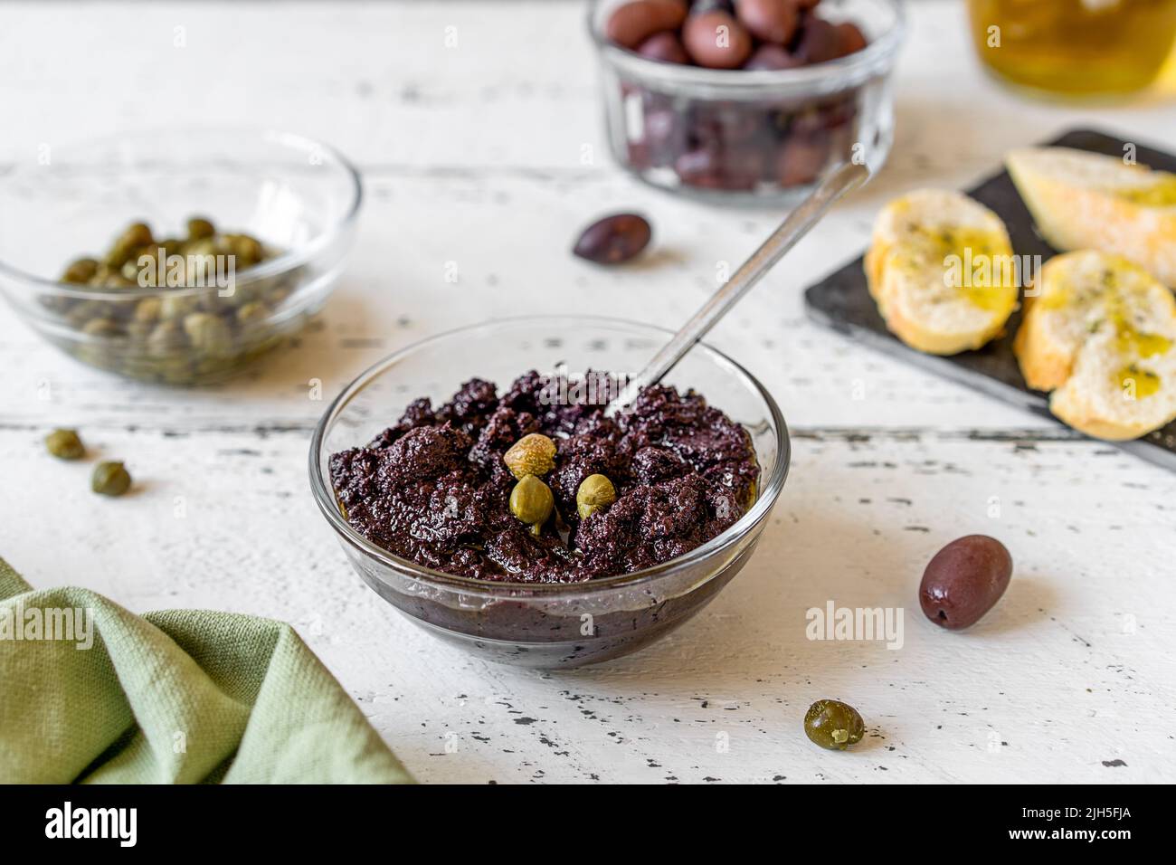 Olive pate in bowl and basic ingredients - olive oil, olives and capers ...