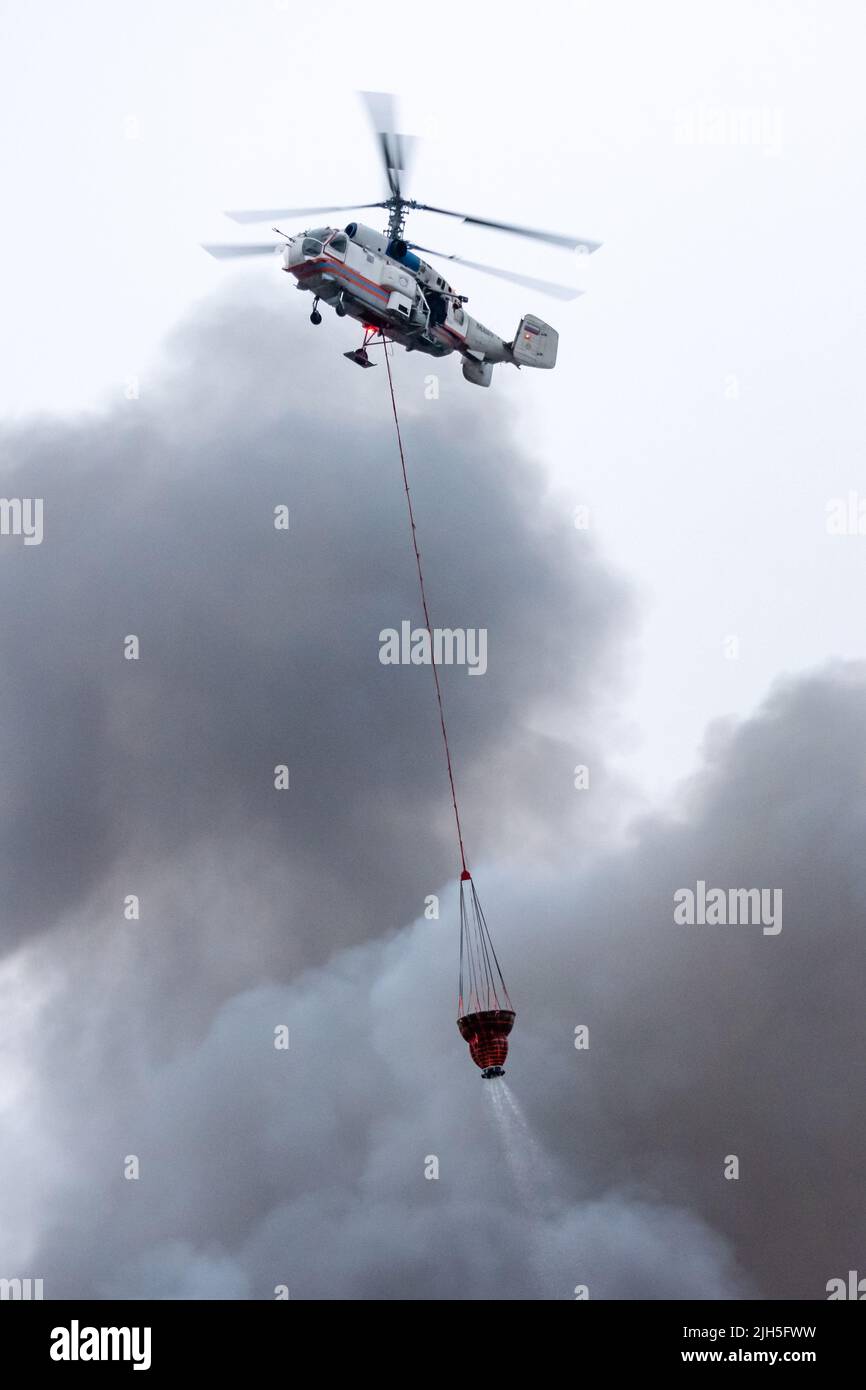 A fire helicopter carries a container of water to extinguish a fire in ...