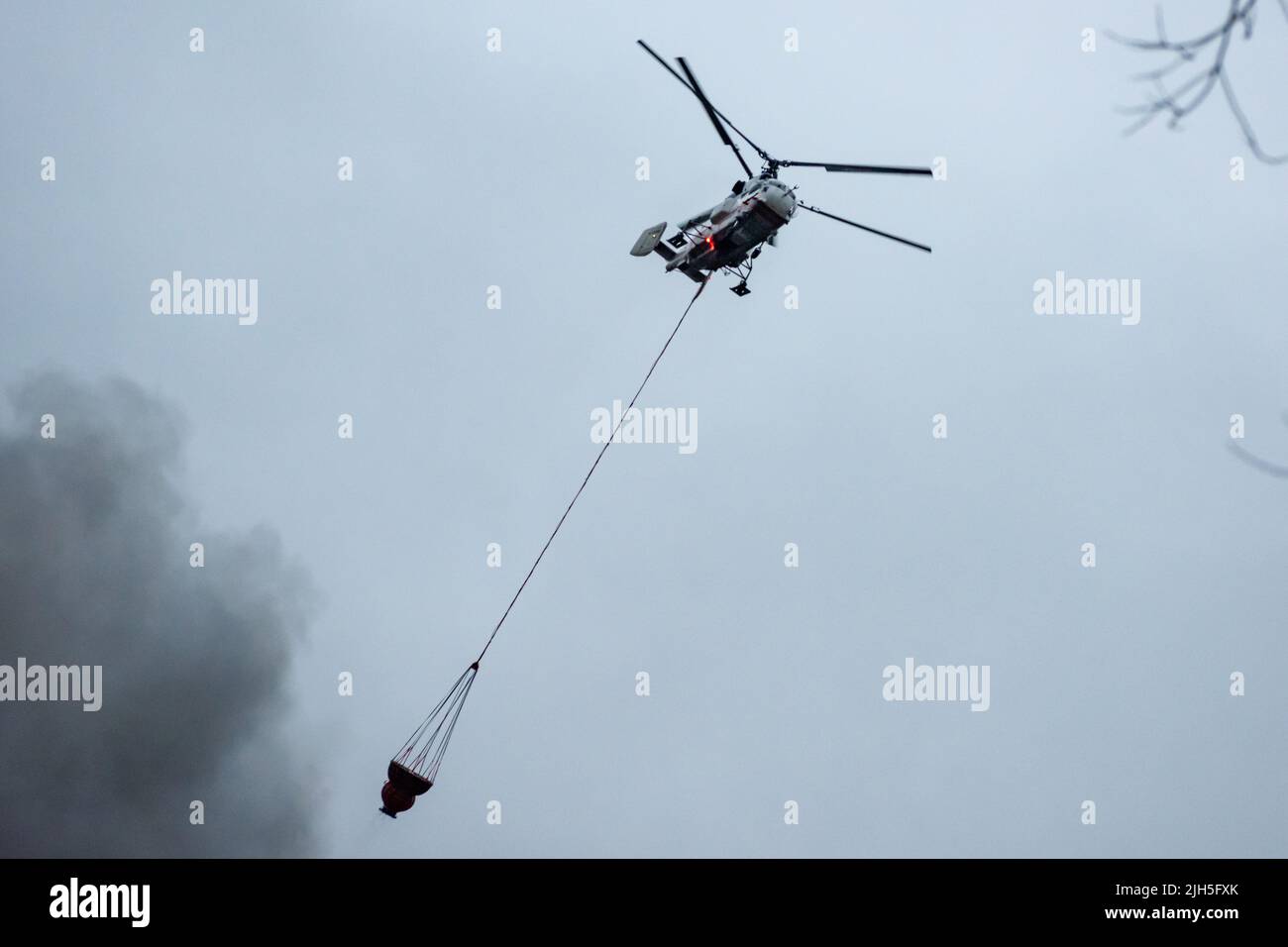 A fire helicopter carries a container of water to extinguish a fire in ...