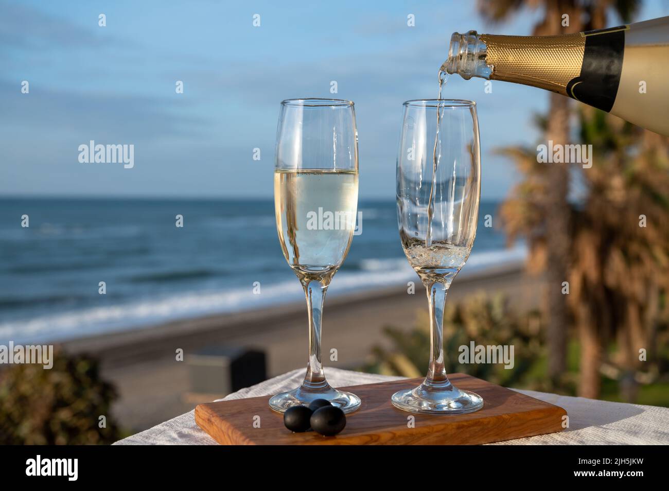 Pouring of Spanish cava sparkling wine is glasses with view on blue sea ...