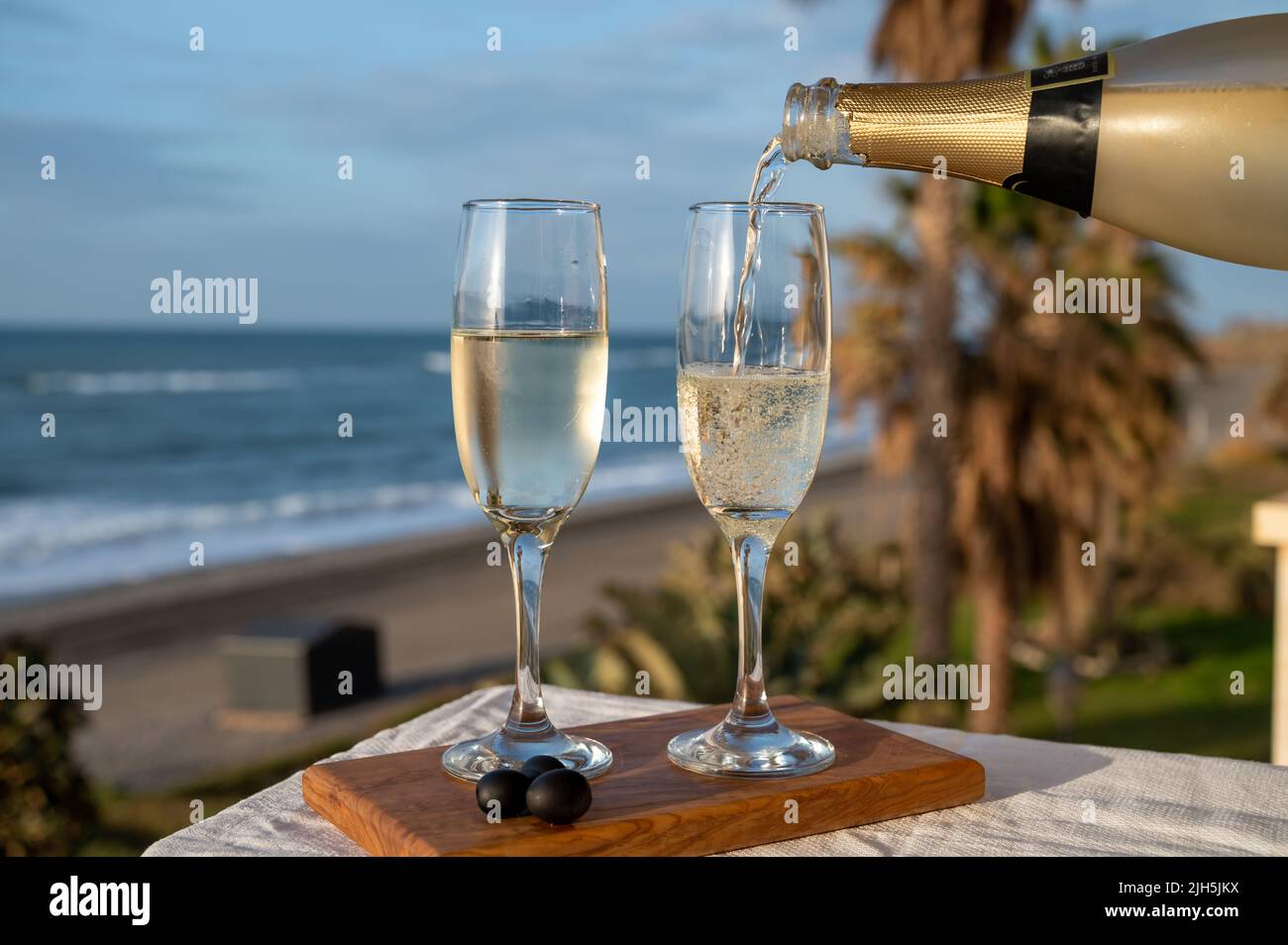 Pouring of Spanish cava sparkling wine is glasses with view on blue sea ...