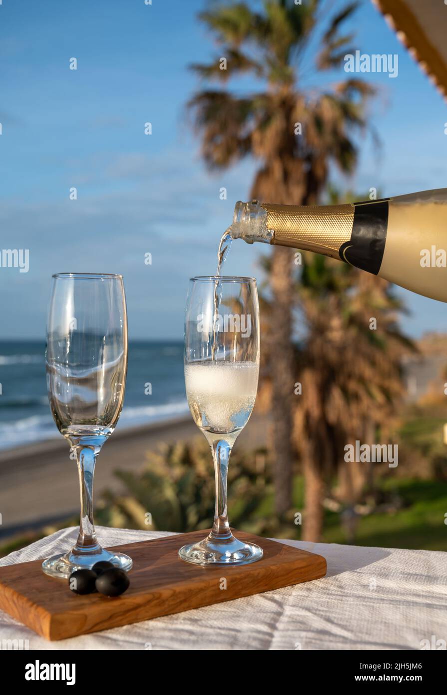 Pouring of Spanish cava sparkling wine is glasses with view on blue sea ...