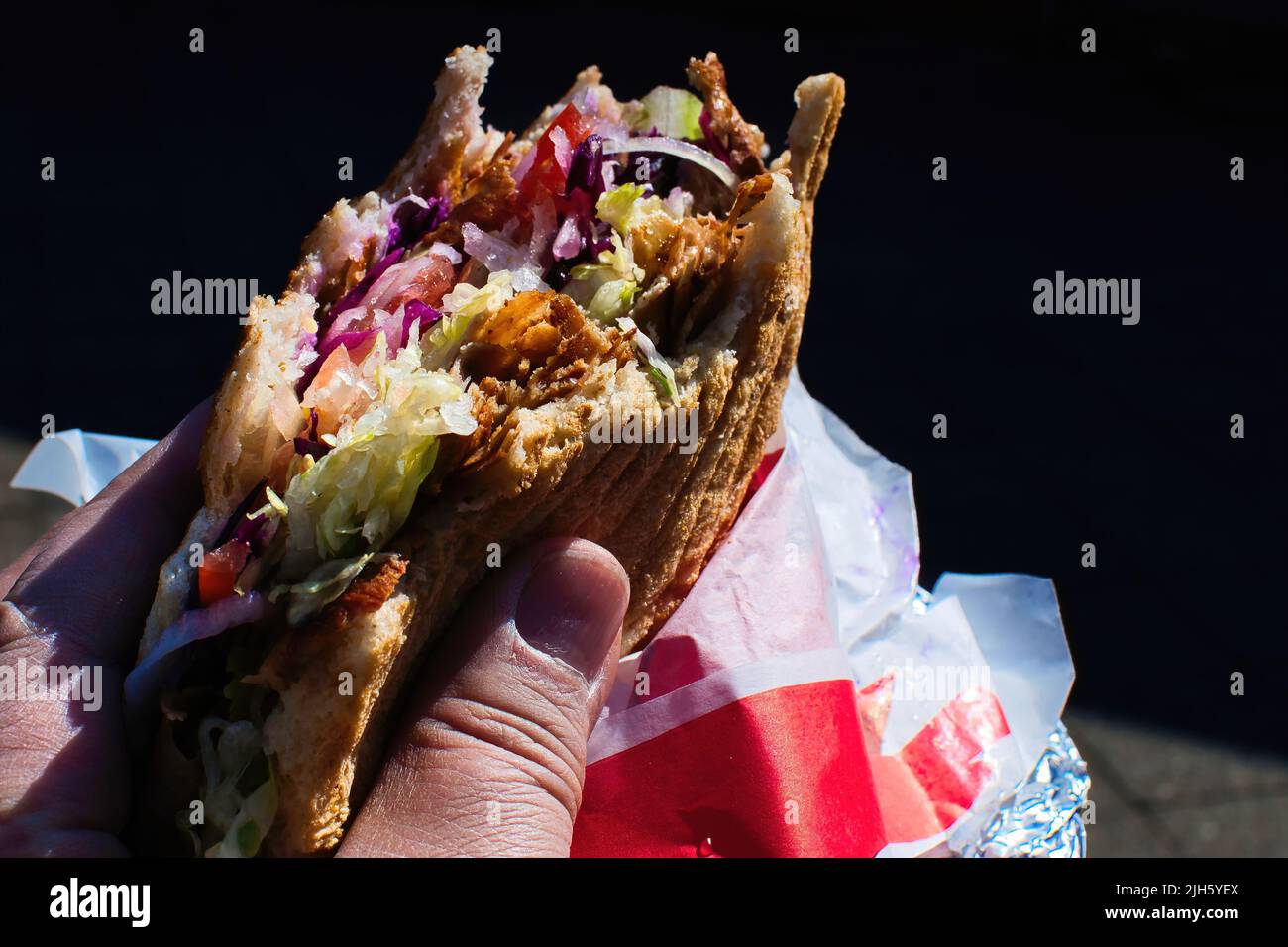 Bitten doner kebab with bread, meat and salad being held in hand Stock ...
