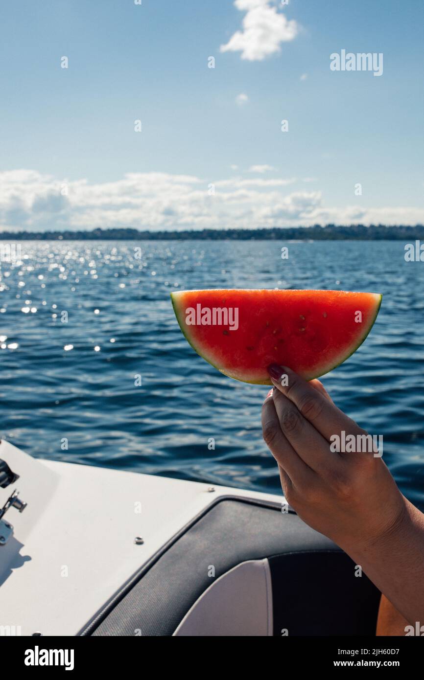 hand holding up watermelon semi circle, half moon with lake, sea, water ...