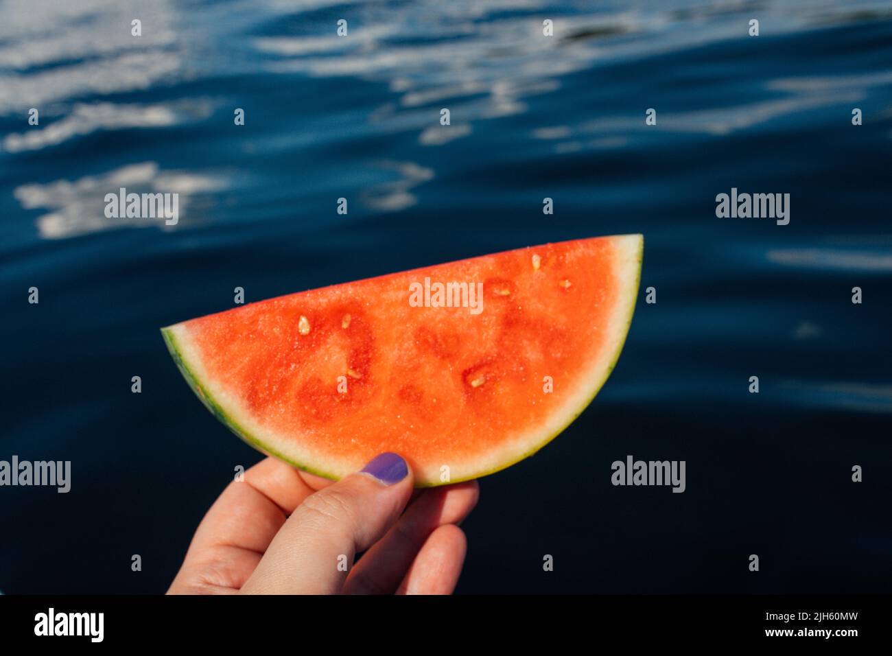 hand holding up watermelon semi circle, half moon with lake, sea, water ...
