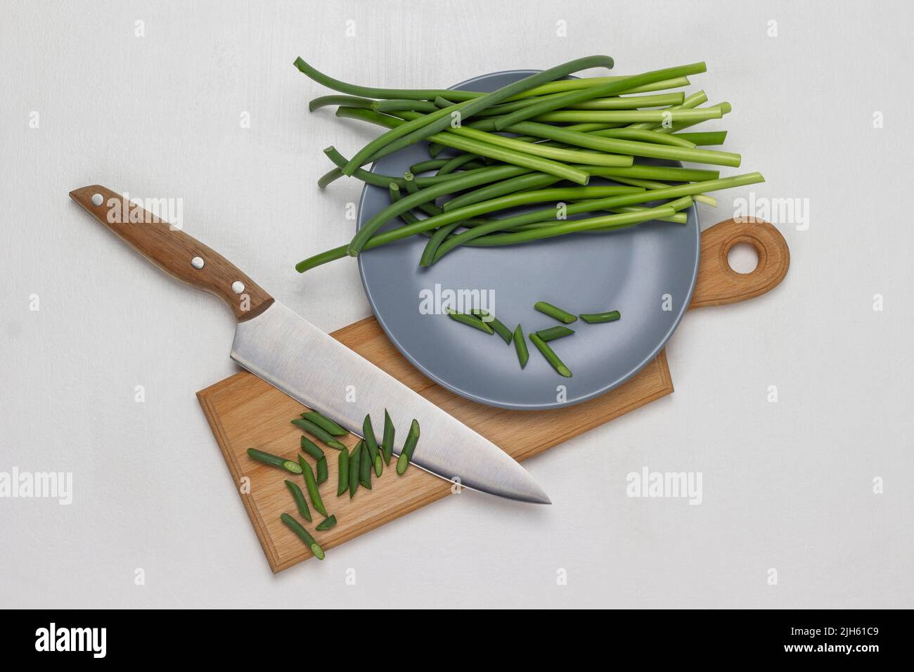 Green pods of garlic on gray plate. Cutting pods of garlic and knife on ...
