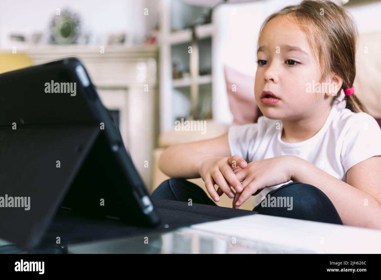 A little blonde girl in front of a tablet, gesturing while watching a ...