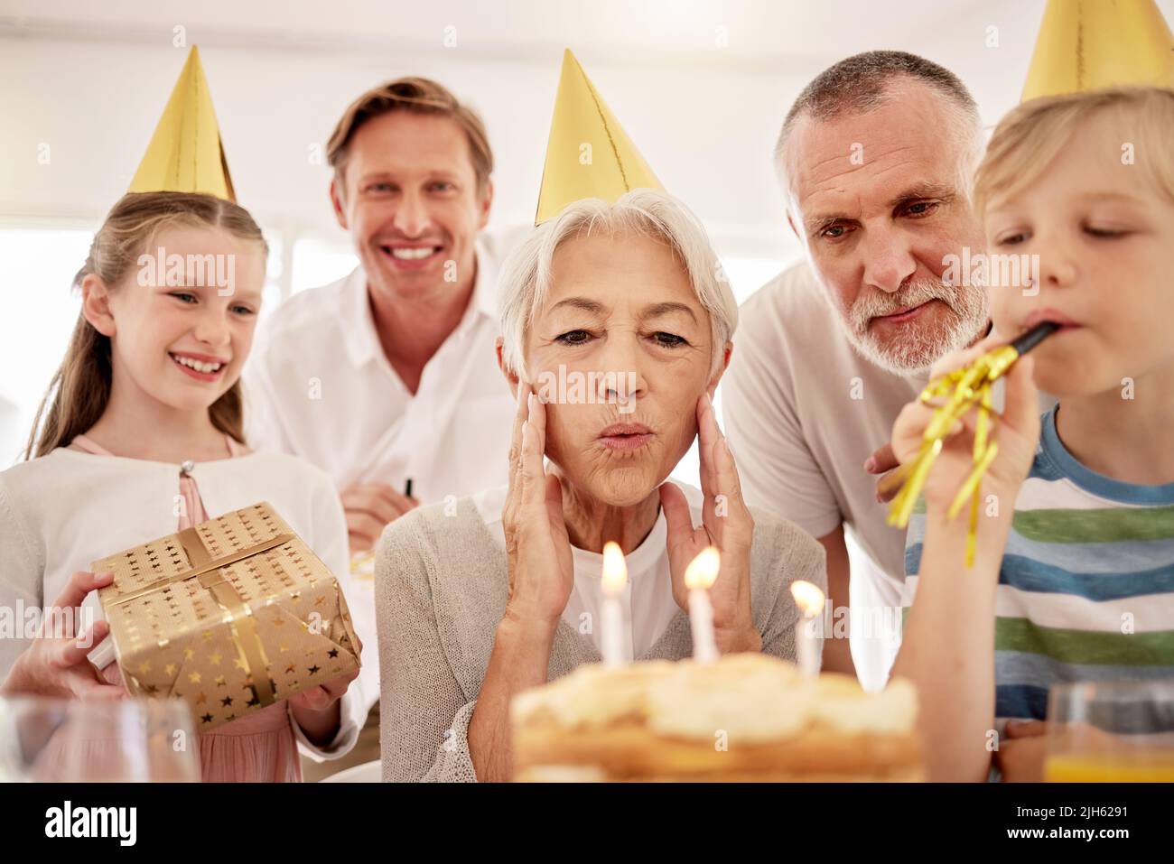 Senior woman celebrating a birthday with family at home, wearing party ...