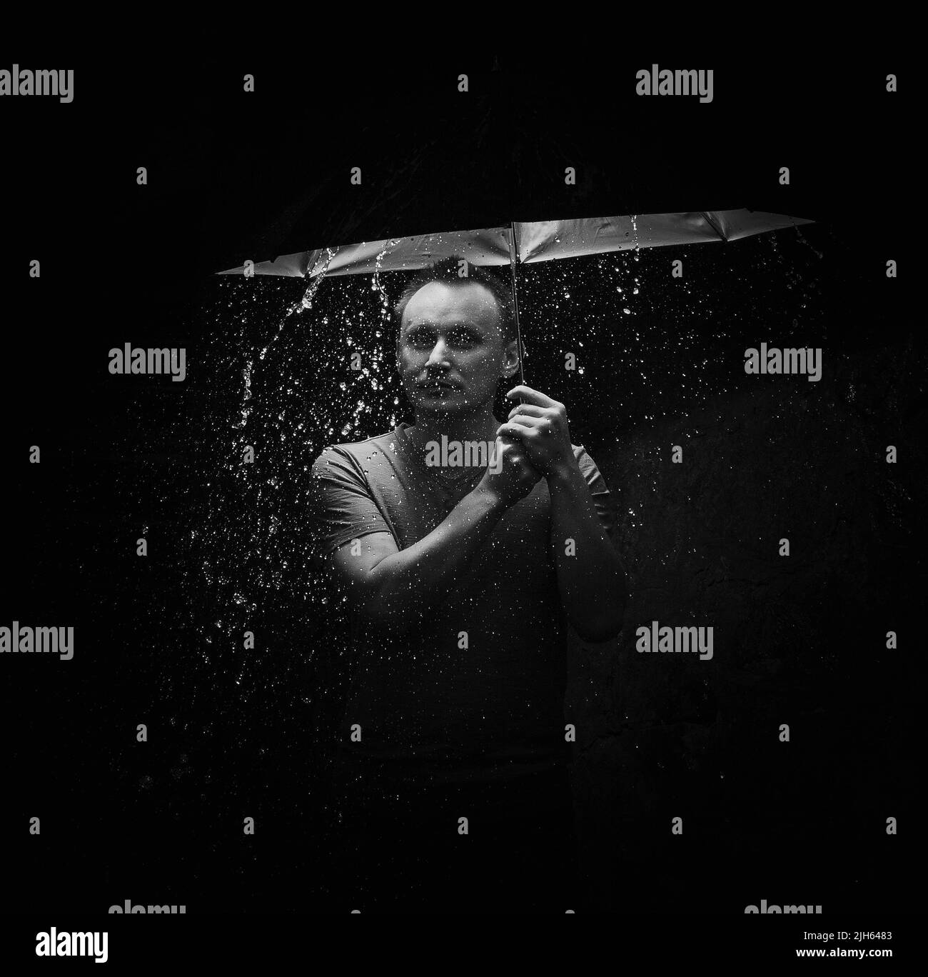 young man standing under umbrella on dark background. It's raining. Light on male Stock Photo ...