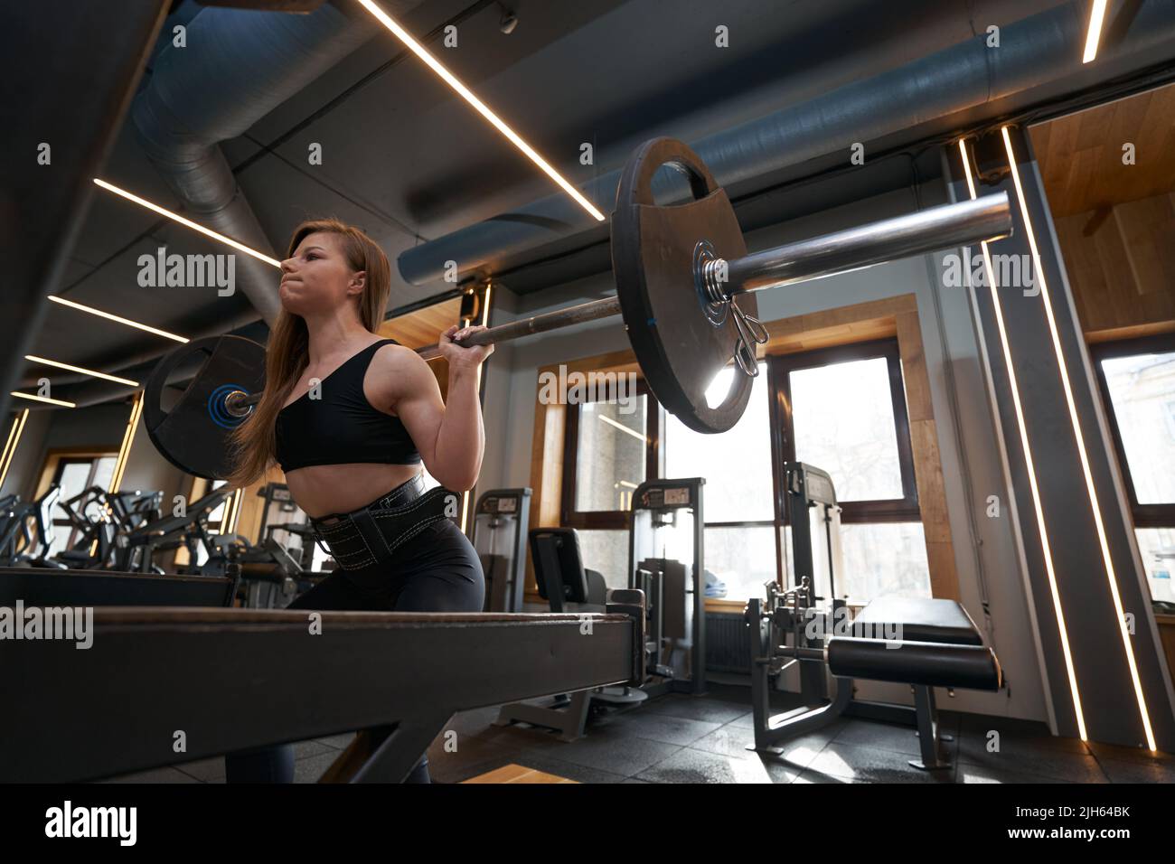 Professional female weightlifter performing barbell exercise indoors ...