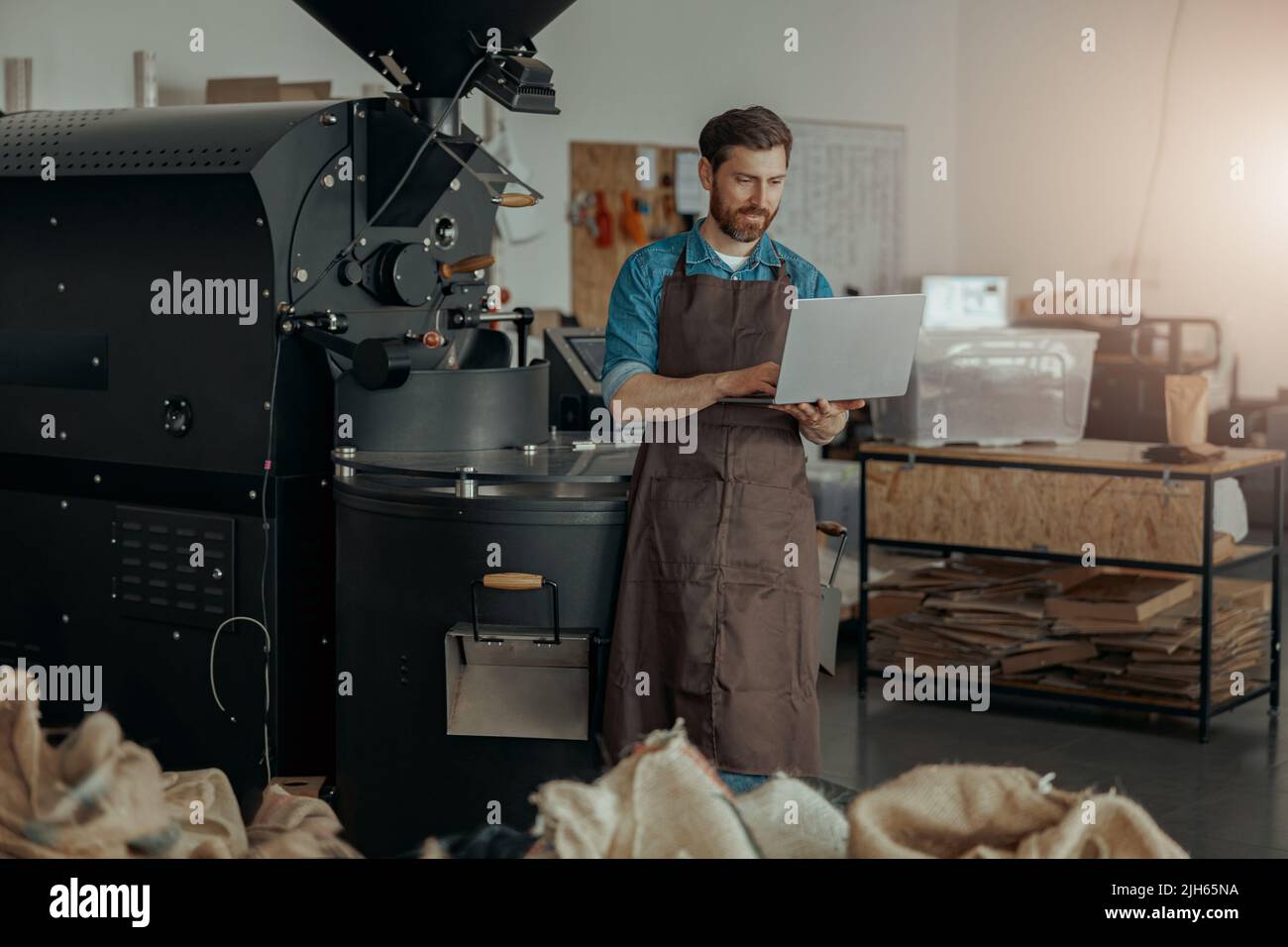 Male worker of small coffee factory working laptop on background of ...