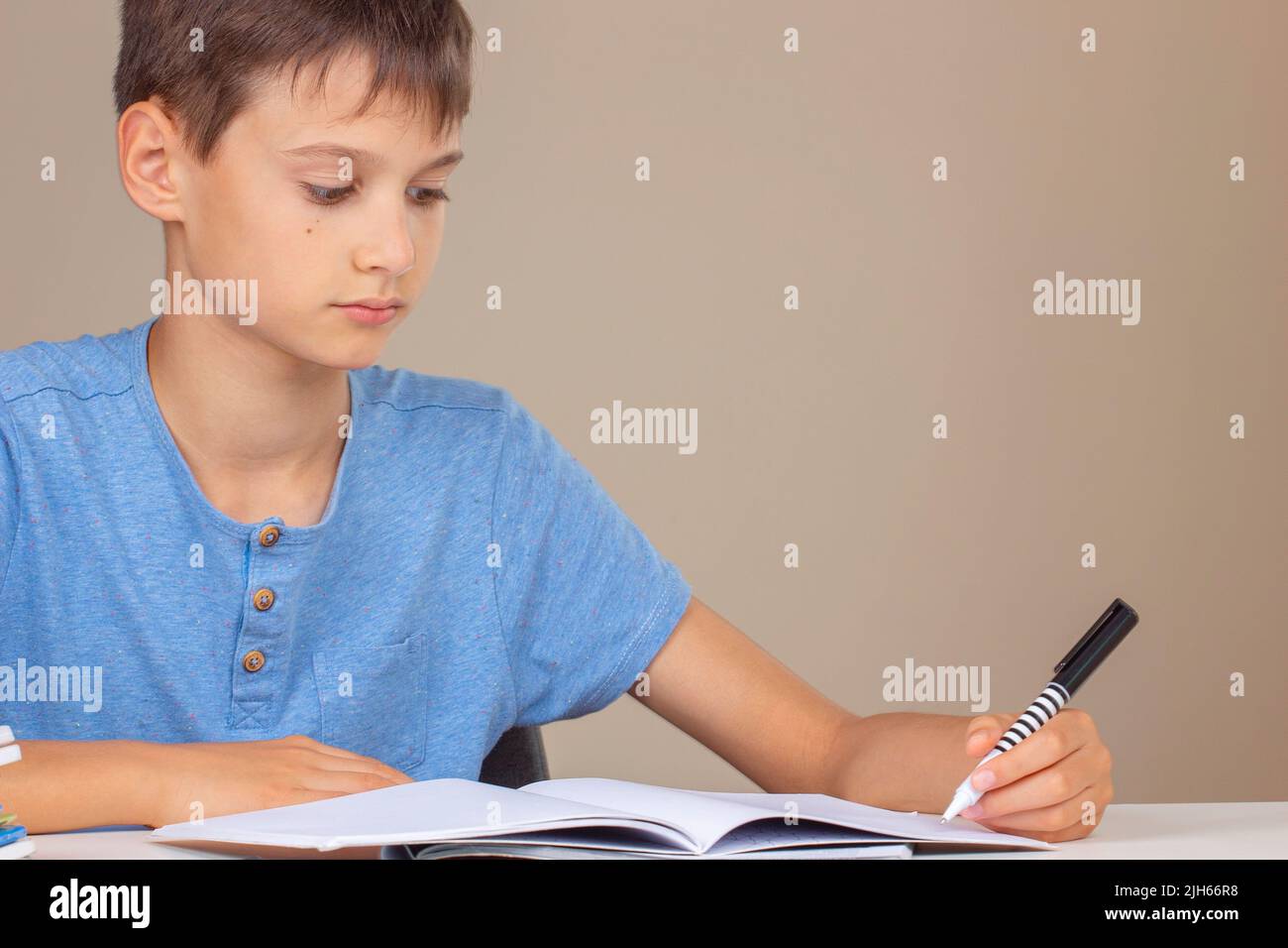 Kid holding pen in left hand and writing in a notebook, doing homework ...