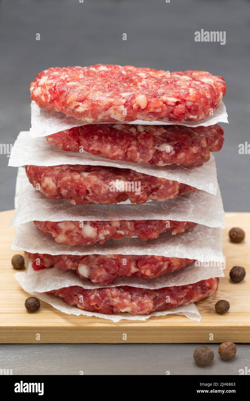 Raw beef burgers are stacked on board. Close up. Grey background Stock ...