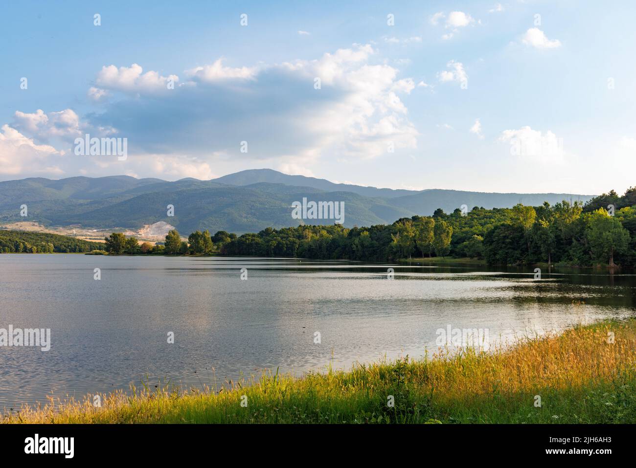 A gleaming wide clear lake reflects bright warm sunlight, against a ...