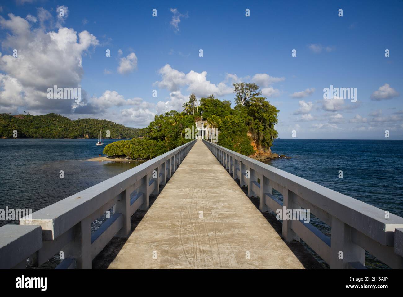 Bridge over the sea to a small green tropical island, blue sky with ...
