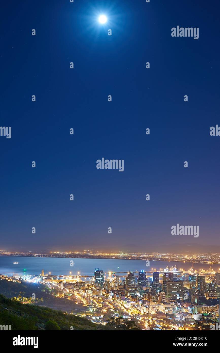 Urban city lights with a full moon in the midnight sky with copy space ...