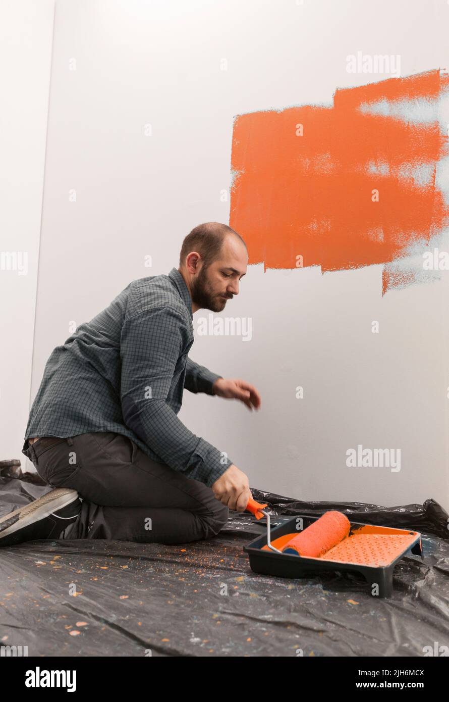 Young adult using orange paint on room wall, doing handmade painting ...